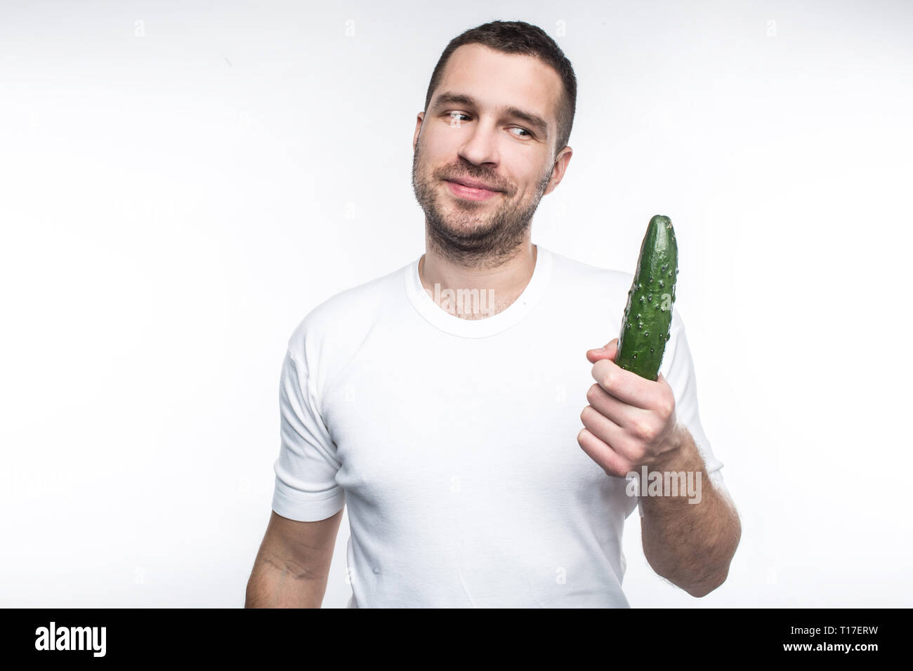 Cheerful and happy guy is holding a big and long cucumber. He likes to ...