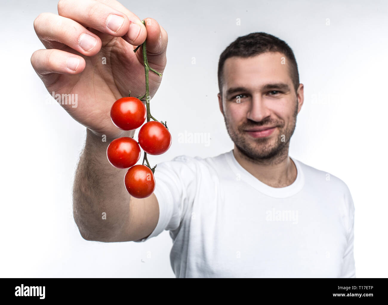 Attractive and handsome man is holding a ramus of cherie tomatoes. This ...
