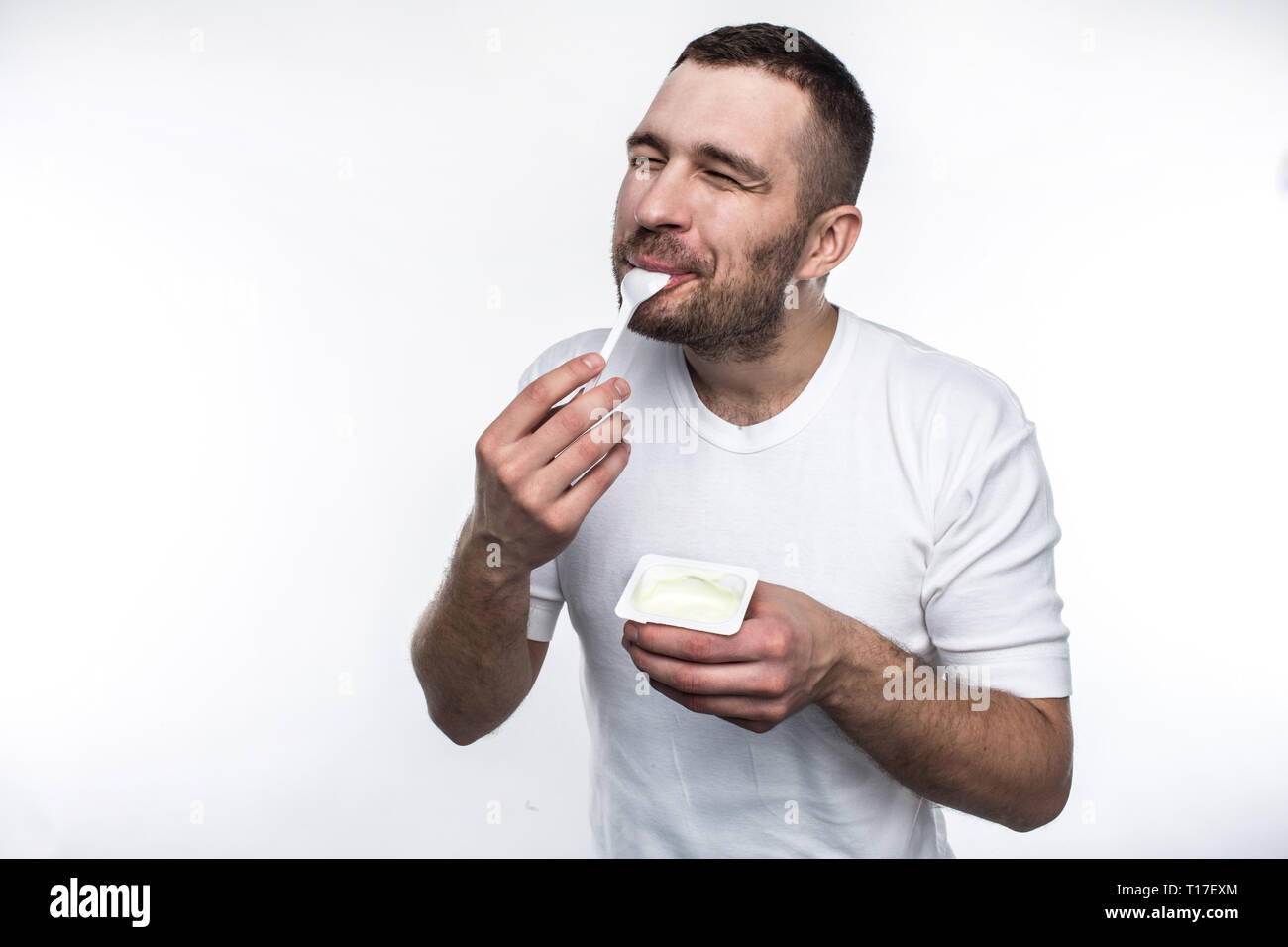 Young and strong man is eating yogurt. He is doing that with pleasure ...