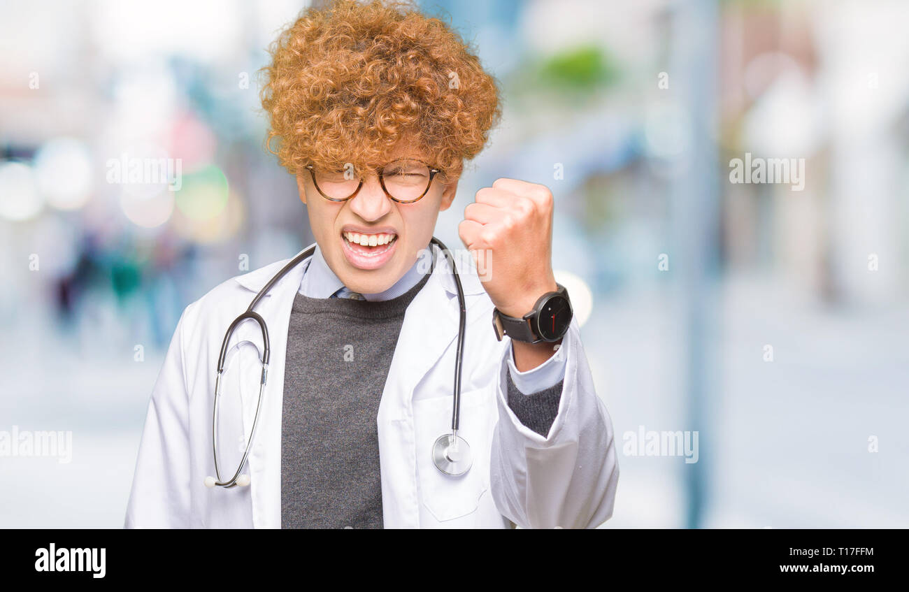Young handsome doctor man wearing medical coat angry and mad raising ...