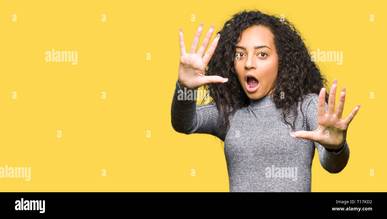 Young beautiful girl with curly hair afraid and terrified with fear ...