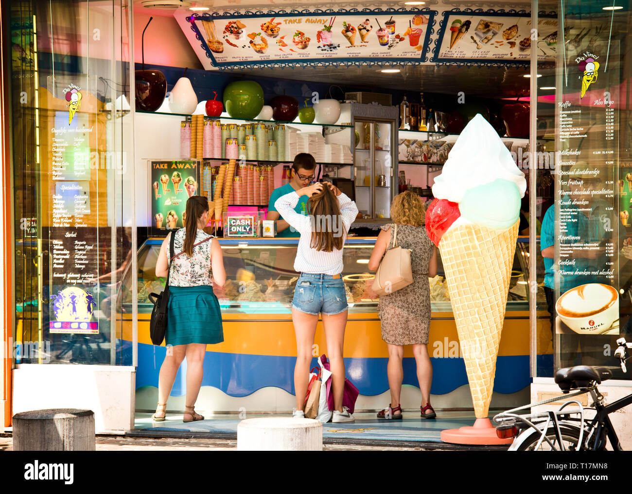 three young women queuing at ice cream parlor purchasing ice cream ...