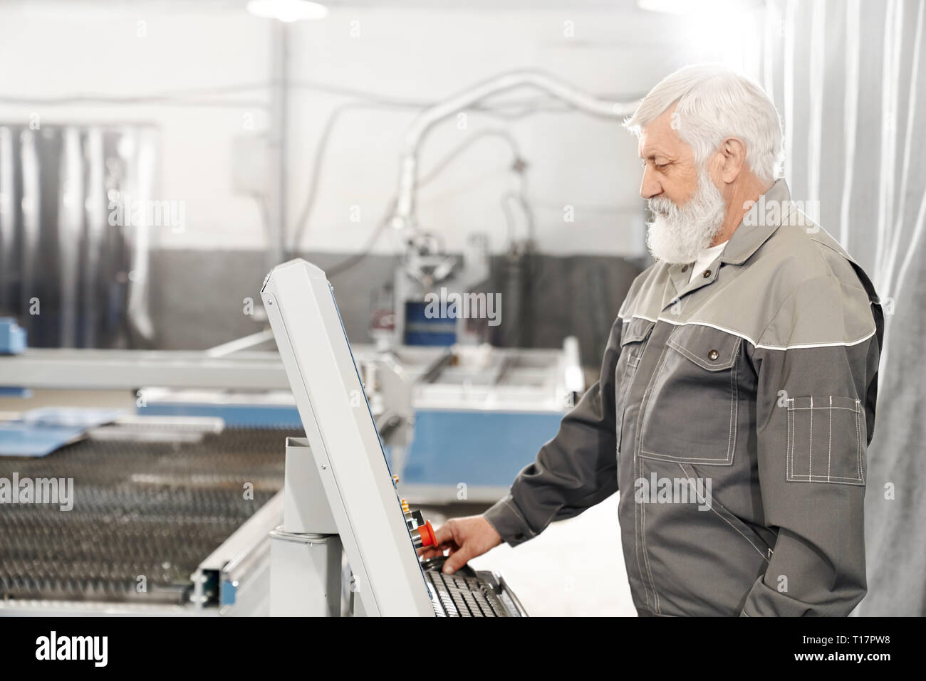 Edlerly bearded man operating laser plasma cutter on metalworking ...