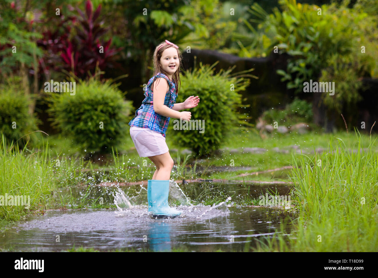 Kid playing out in the rain. Children with umbrella and rain boots play ...