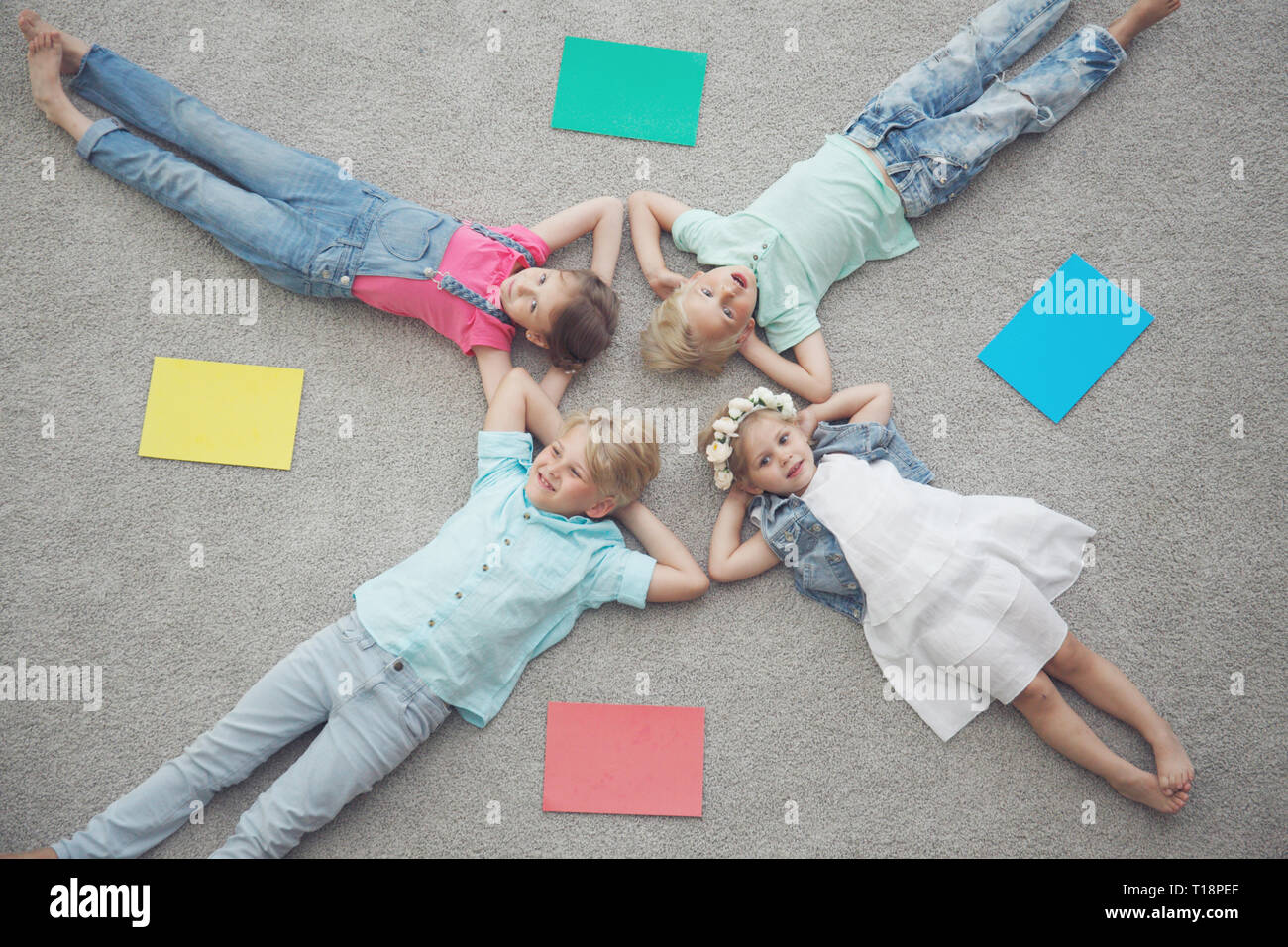 Four happy children laying on floor and smiling among colorful paper ...