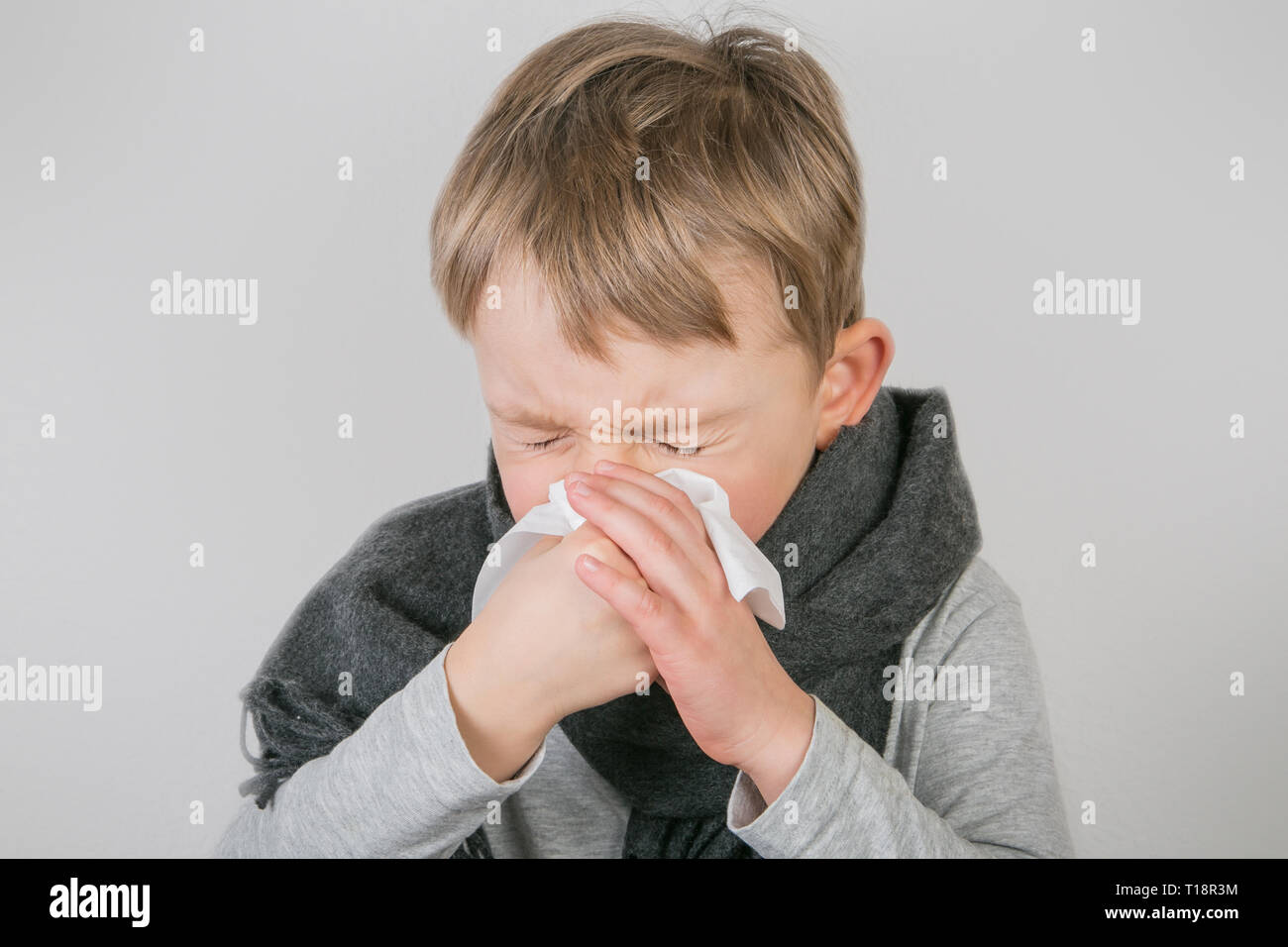 Sick boy sneezes, grey background Stock Photo - Alamy