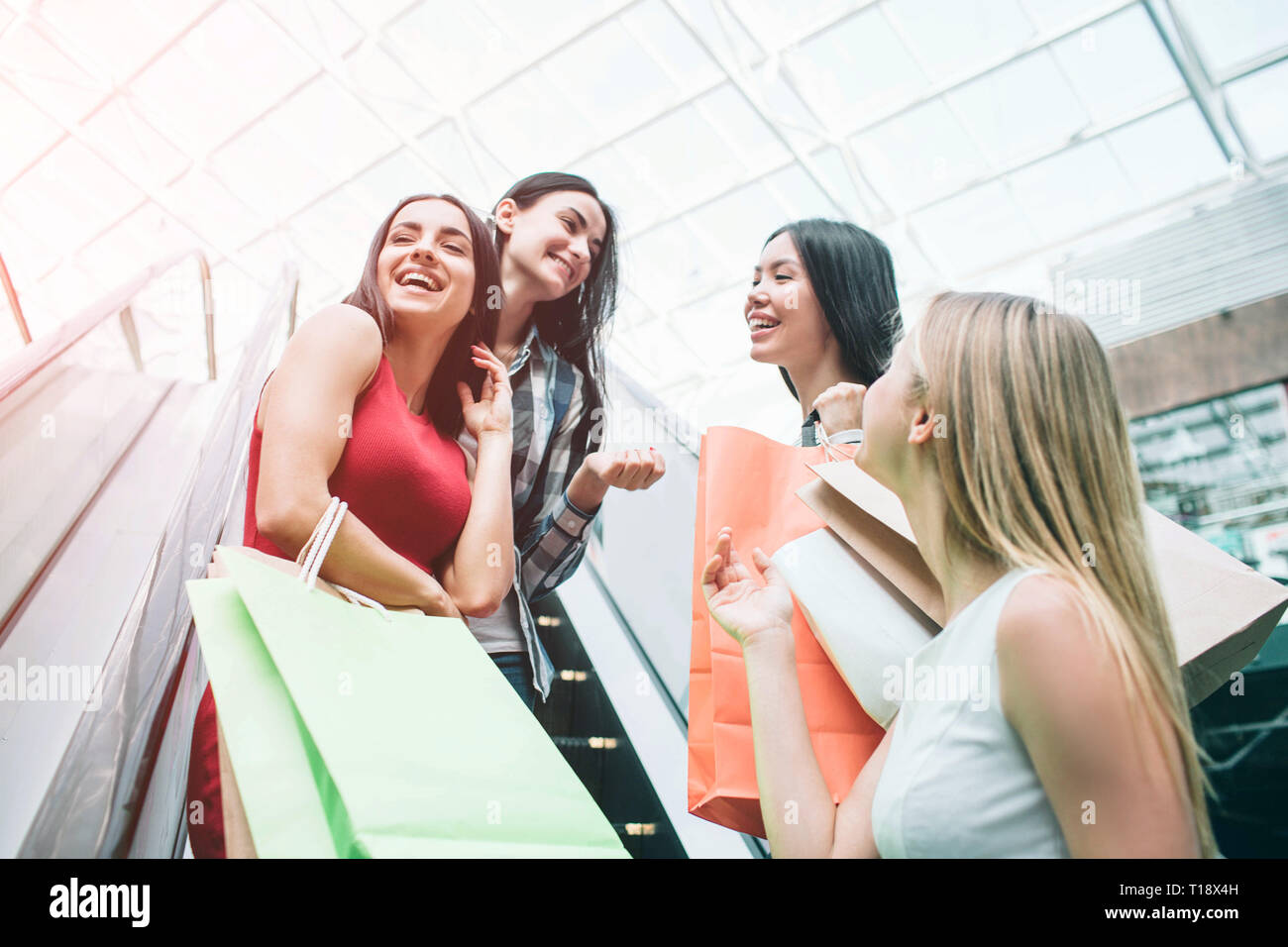 Pretty and happy girls are standing on escalator and laughing. They are ...