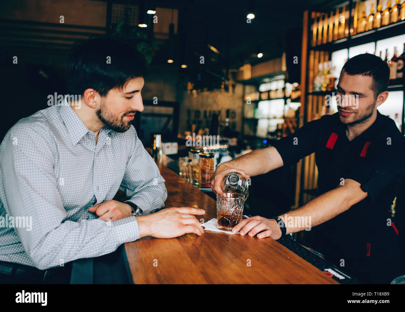 Customer sitting at the barman's stand and looking how barmen is ...