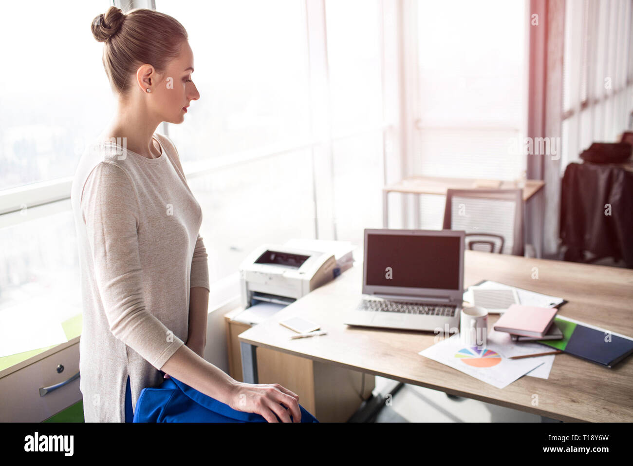 A picture of busy woman standing near her office table and chair. She ...