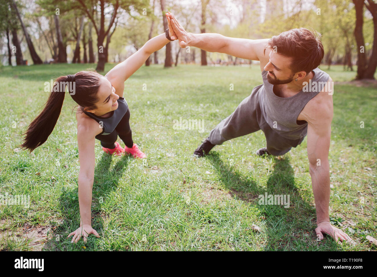 Slim and well-built people are exercising on grass in park. They are ...