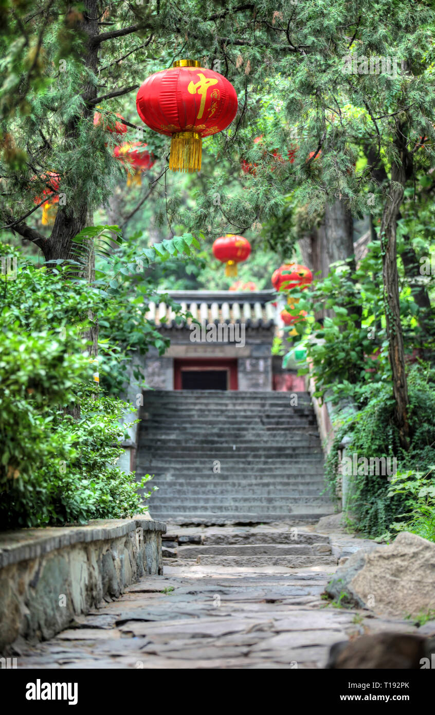 Lanterns hang over a smooth stone path leading to steps up to a temple ...