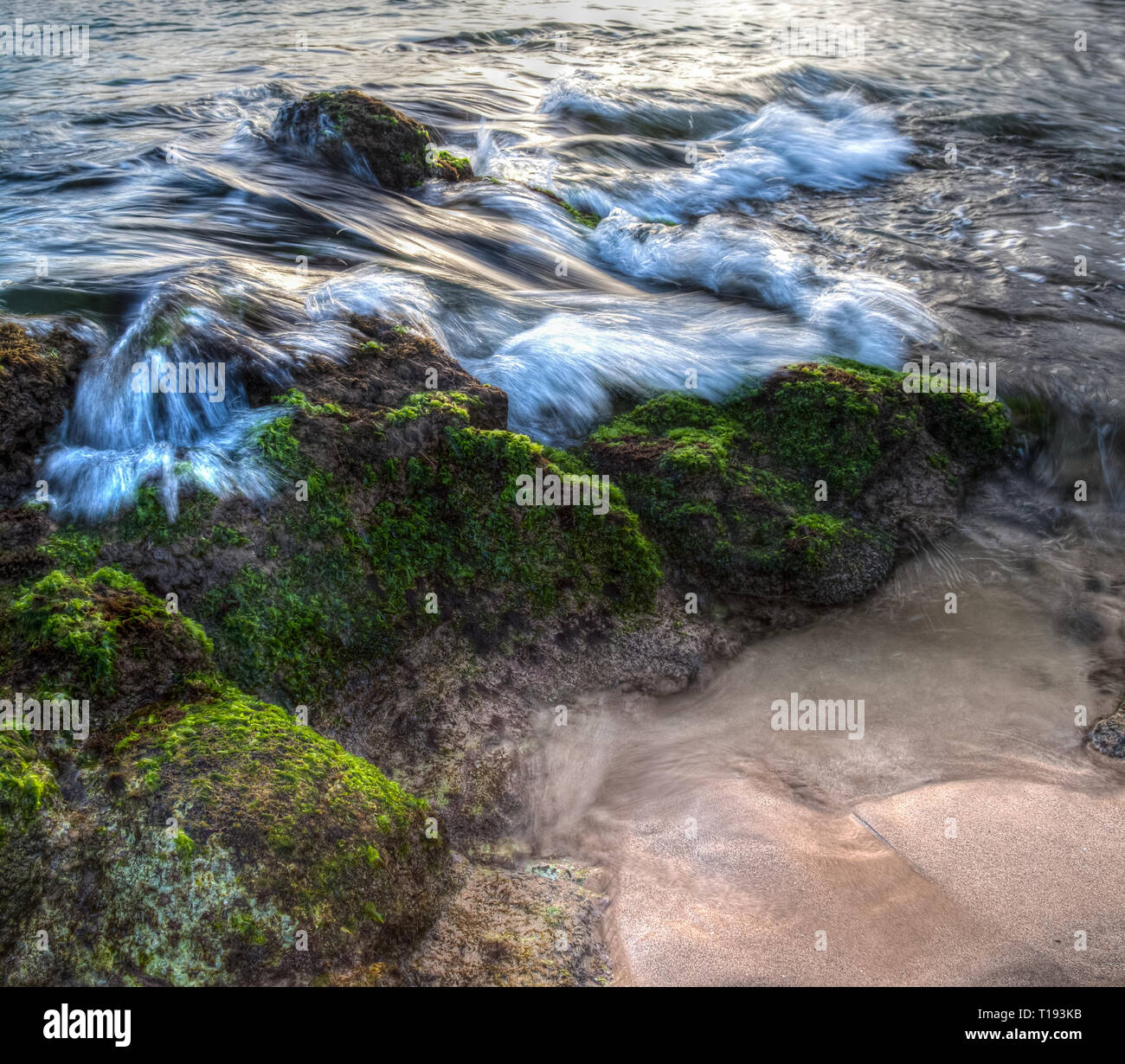 Smooth waves gently wash over rocks at a beach in Kauai Hawaii Stock ...
