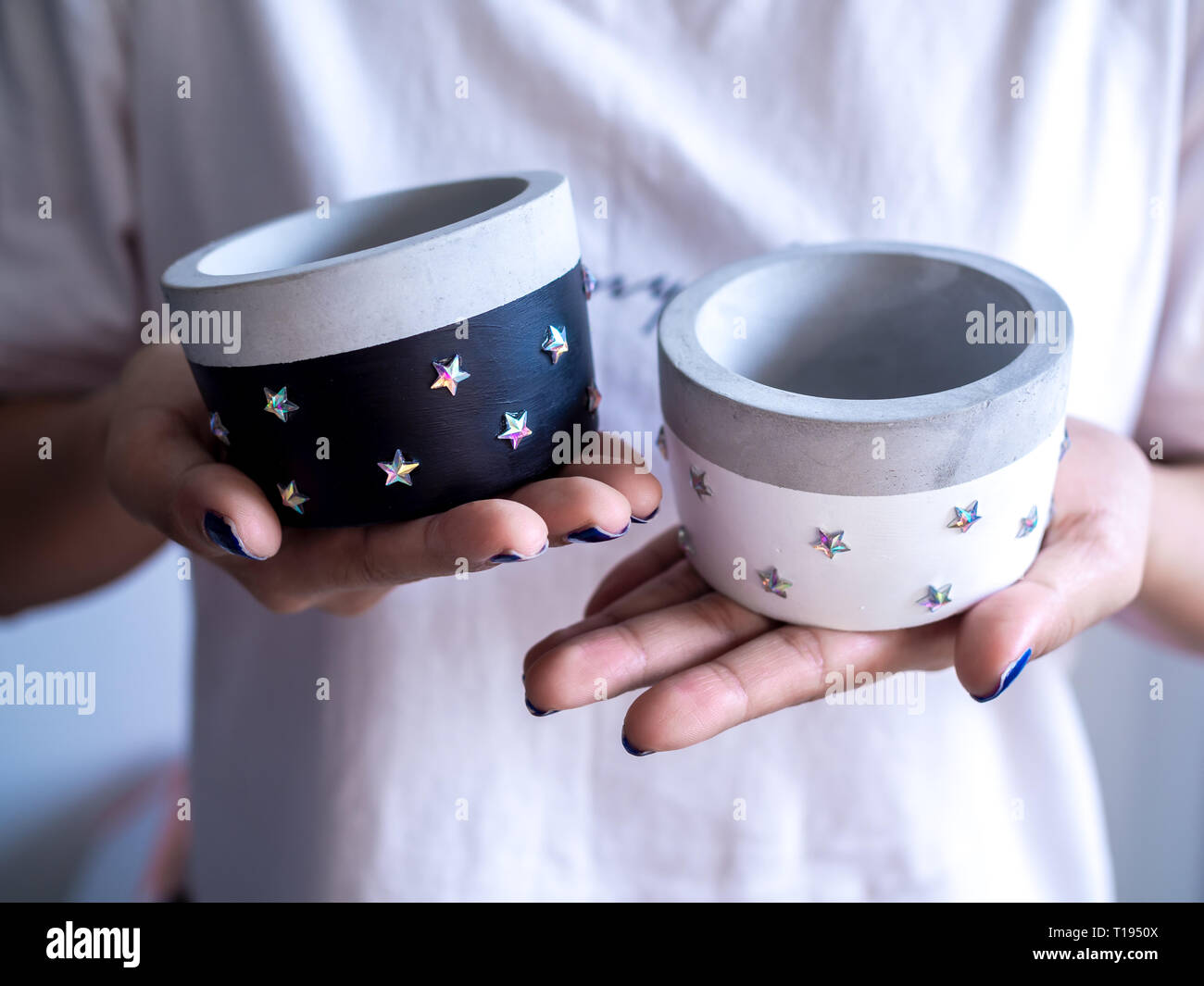 Hands holding empty black and white modern round concrete planters with ...