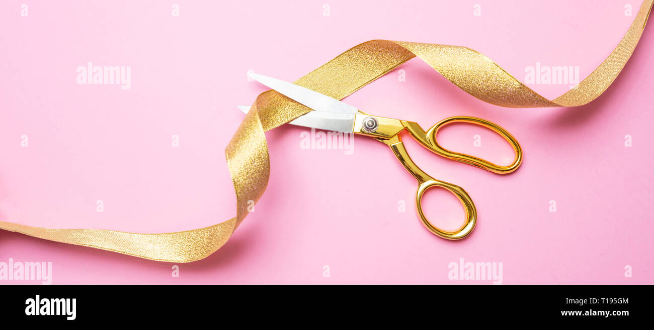 Grand opening concept. Gold scissors cutting golden ribbon against pink ...
