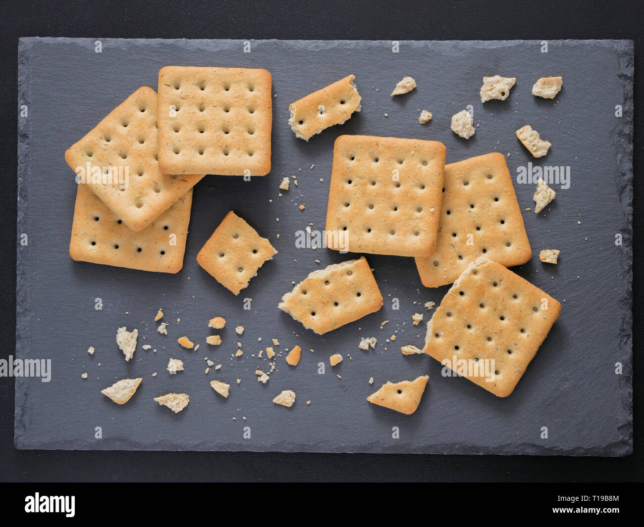 Square crackers with pieces and crumbs on slate gray background. Dry ...