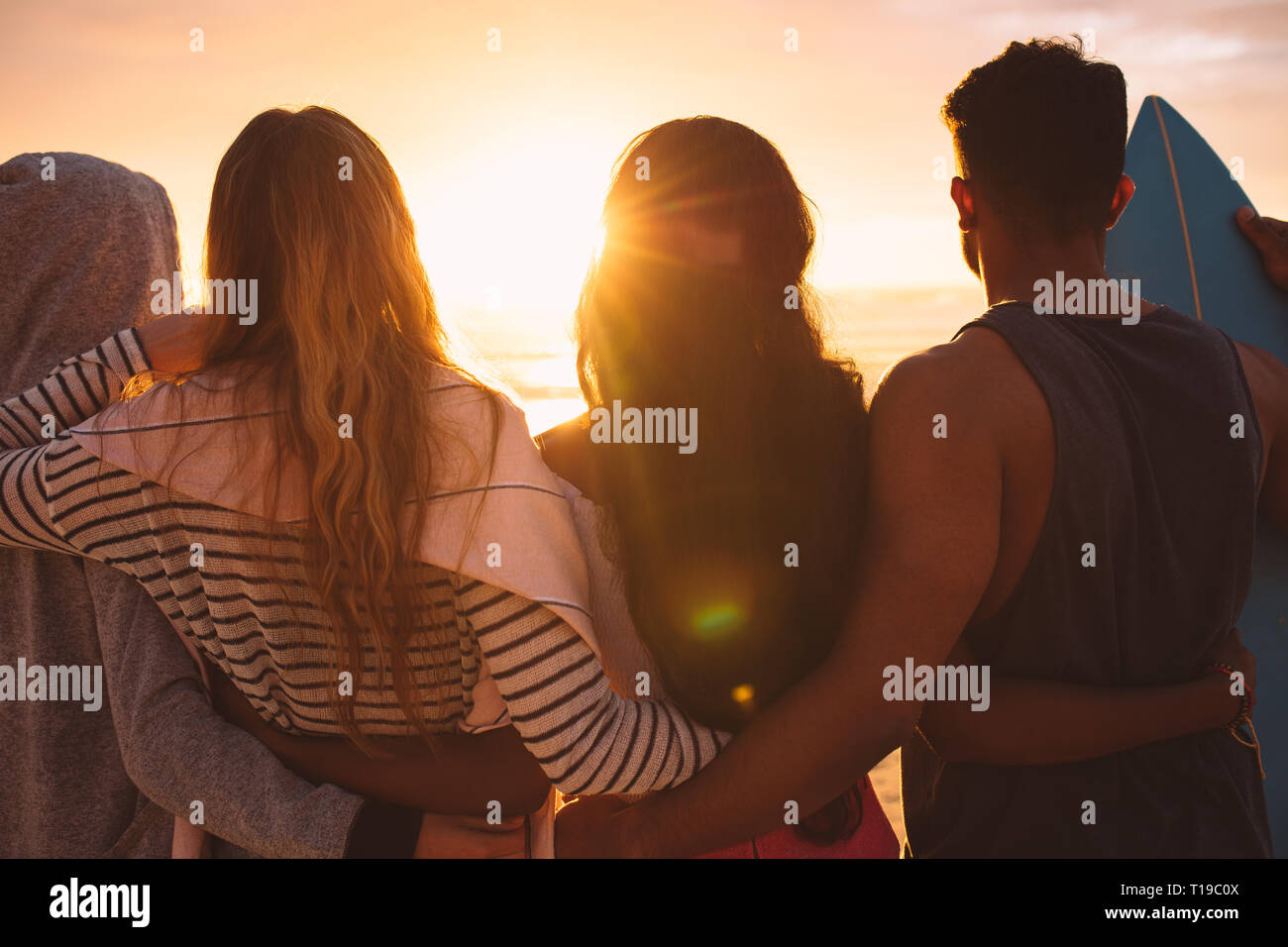 Rear view of a group of friends standing together on beach holding each ...