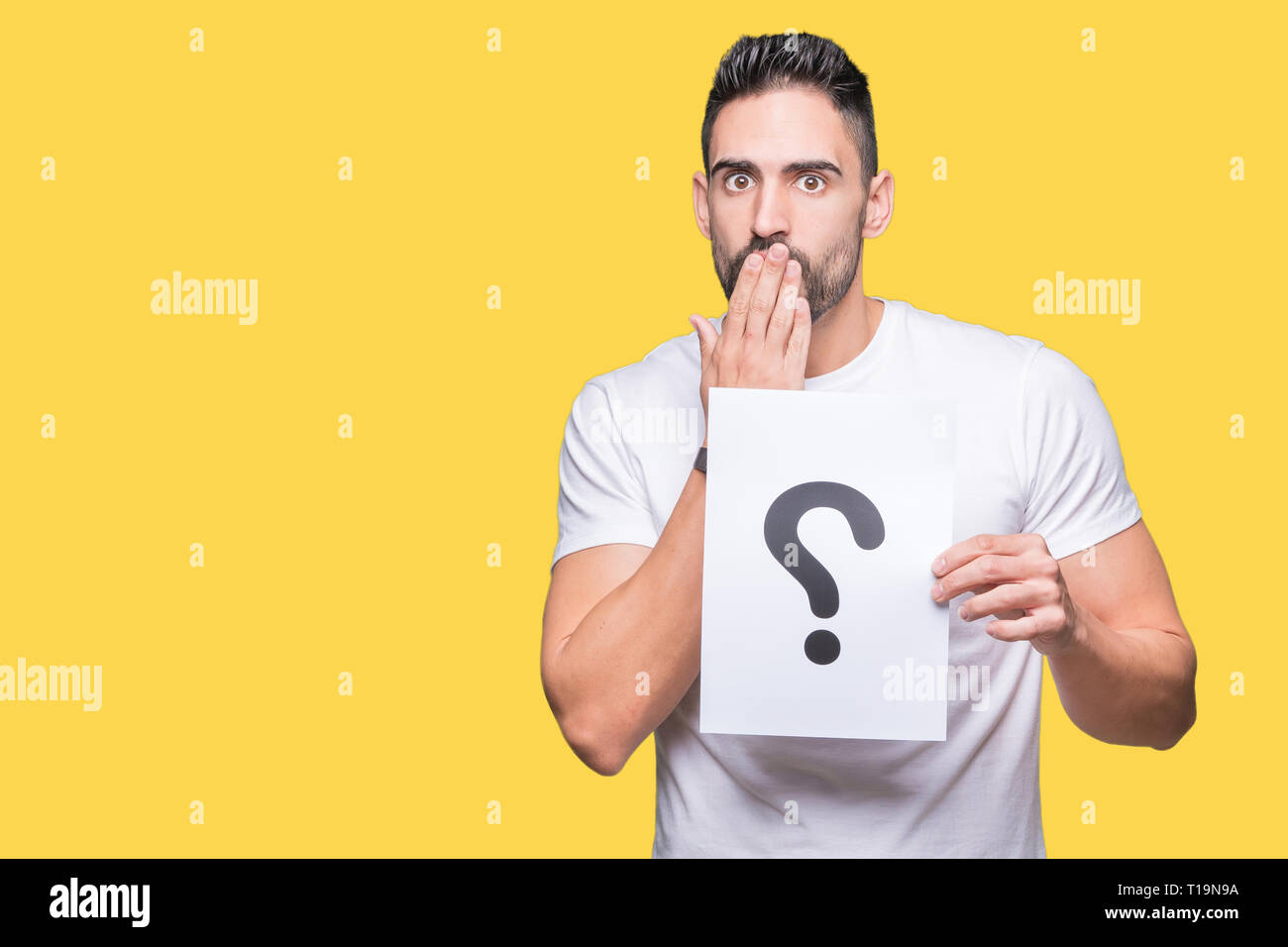 Handsome young man holding paper with question mark over isolated ...