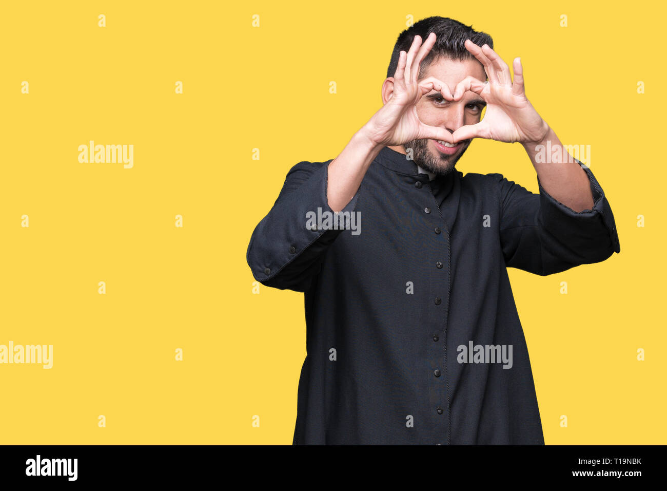 Young Christian priest over isolated background Doing heart shape with ...