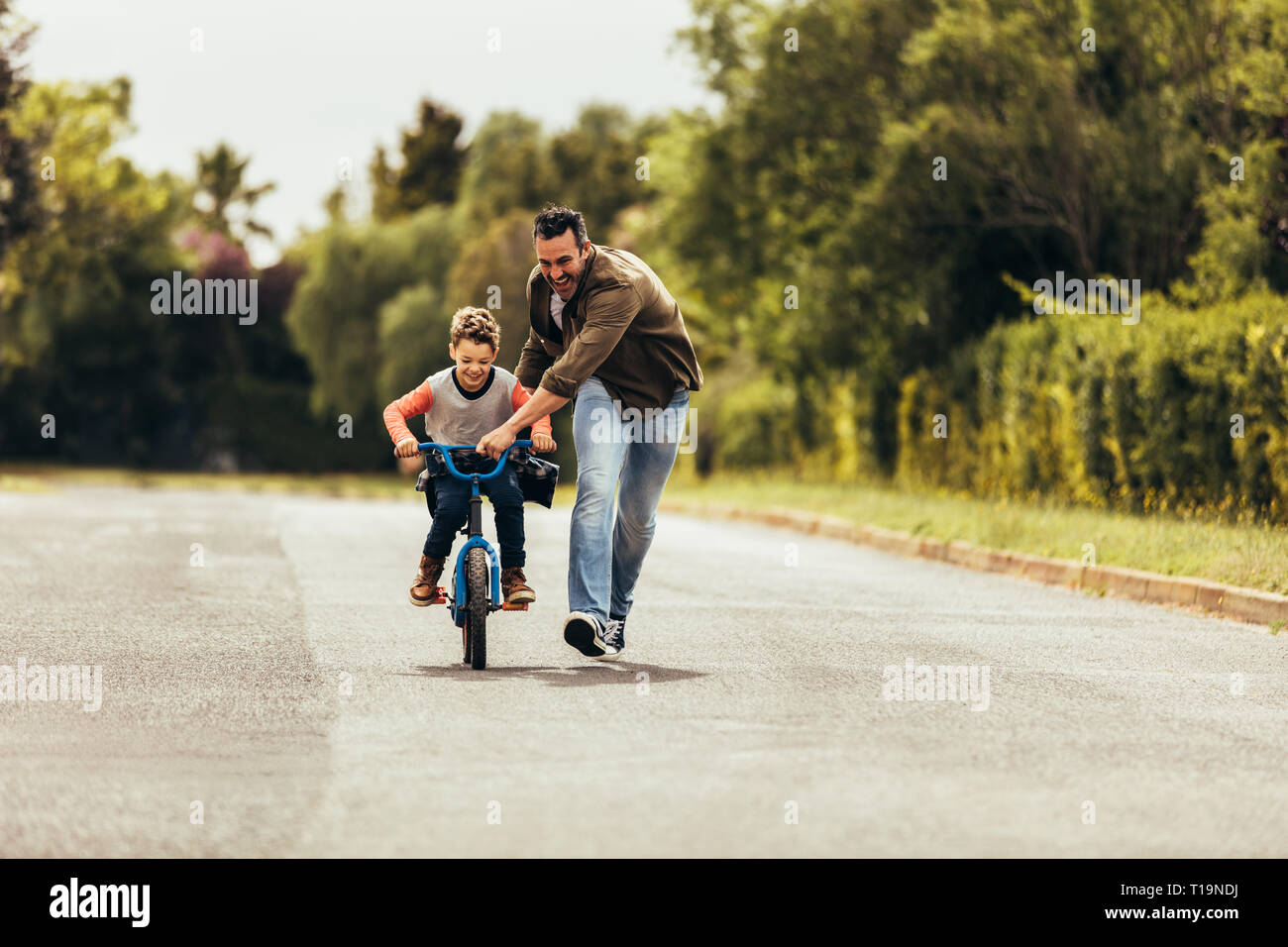 Kid riding a bicycle while his father runs along holding the bicycle ...
