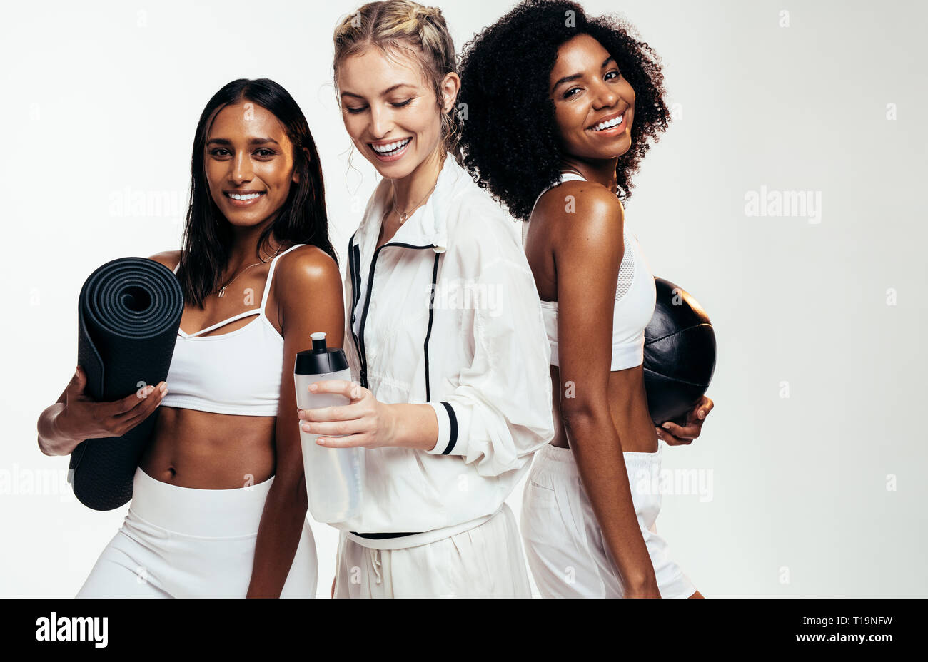 Three young woman in sportswear standing together over white background ...