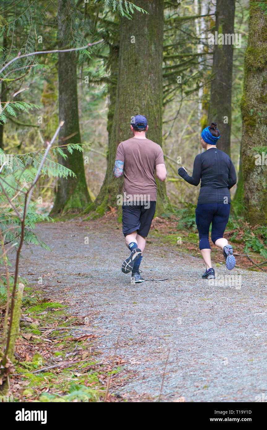 Young couple running on a trail in a forested area of Cliff Falls Park ...