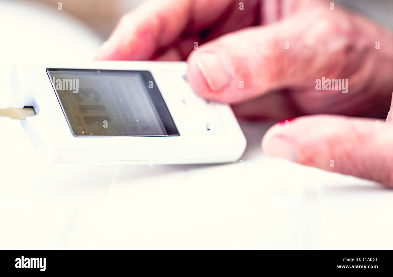 Small portable digital blood glucose meter use by a senior man diabetic ...