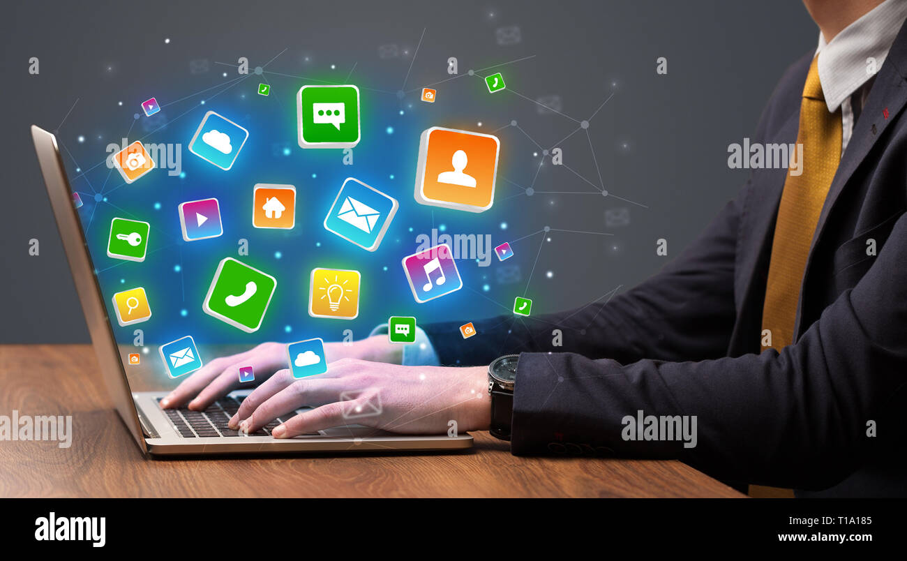Businessman hand typing on laptop with flying application icons around ...