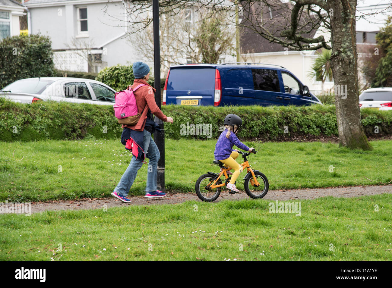 A mother following her young daughter cycling in a park Stock Photo - Alamy