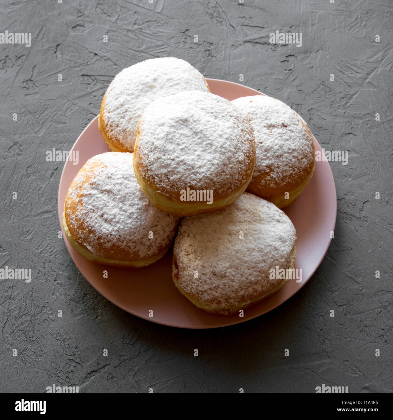 Homemade sweet donuts with powdered sugar on pink plate over concrete ...