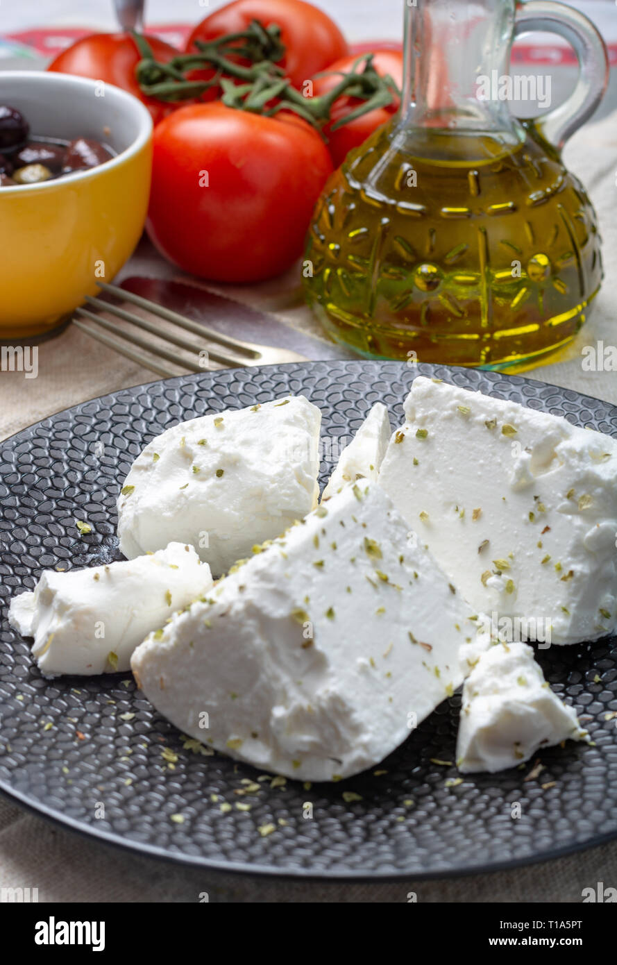 Fresh young soft white salted Feta cheese on black plate seasoned with ...