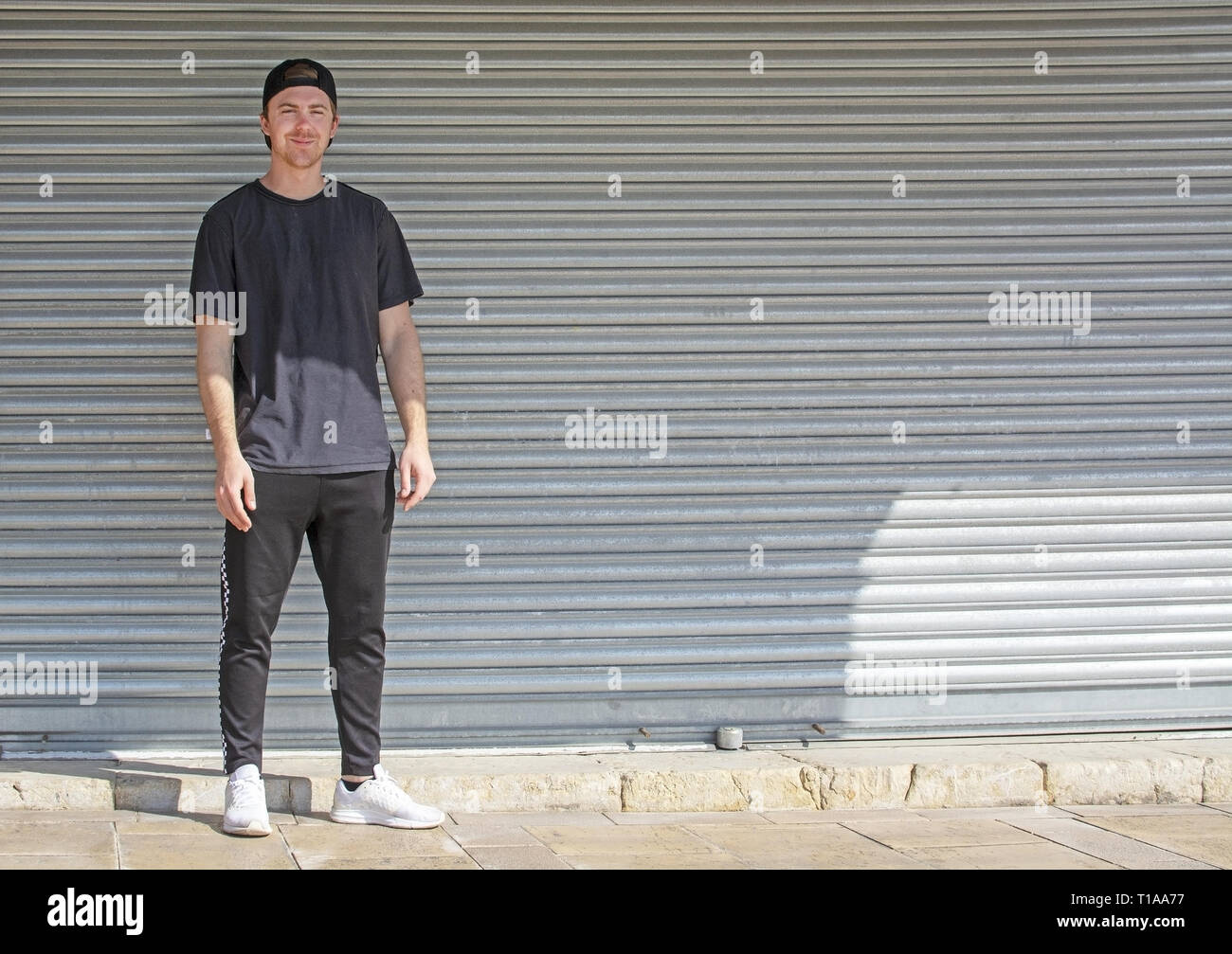 Young casual sporty dressed man with cap backwards in black against ...
