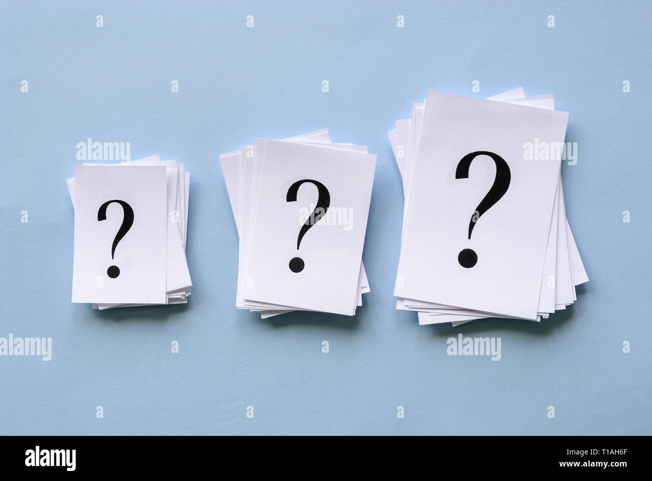 Three piles of question marks printed on white paper in different sizes ...