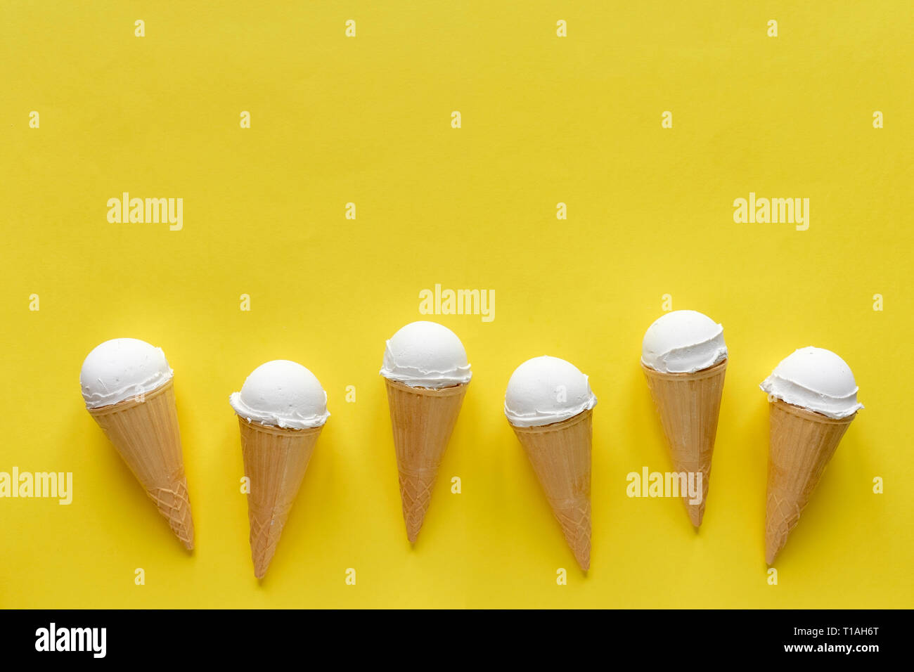 Row of six vanilla ice cream cones on yellow forming a lower border ...