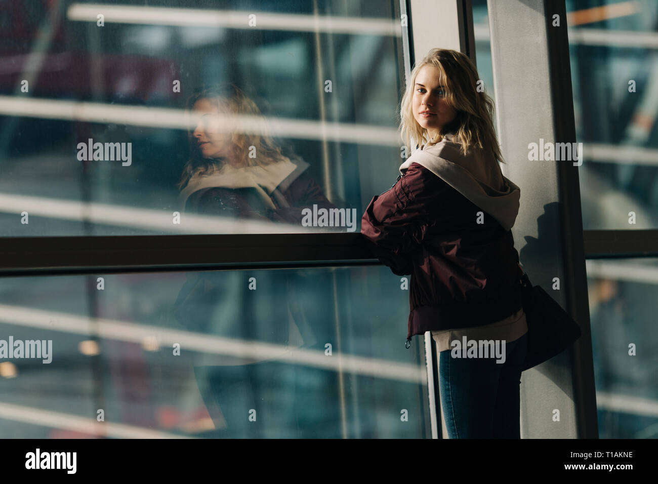 Photo of blonde in jacket standing against windows in building Stock ...