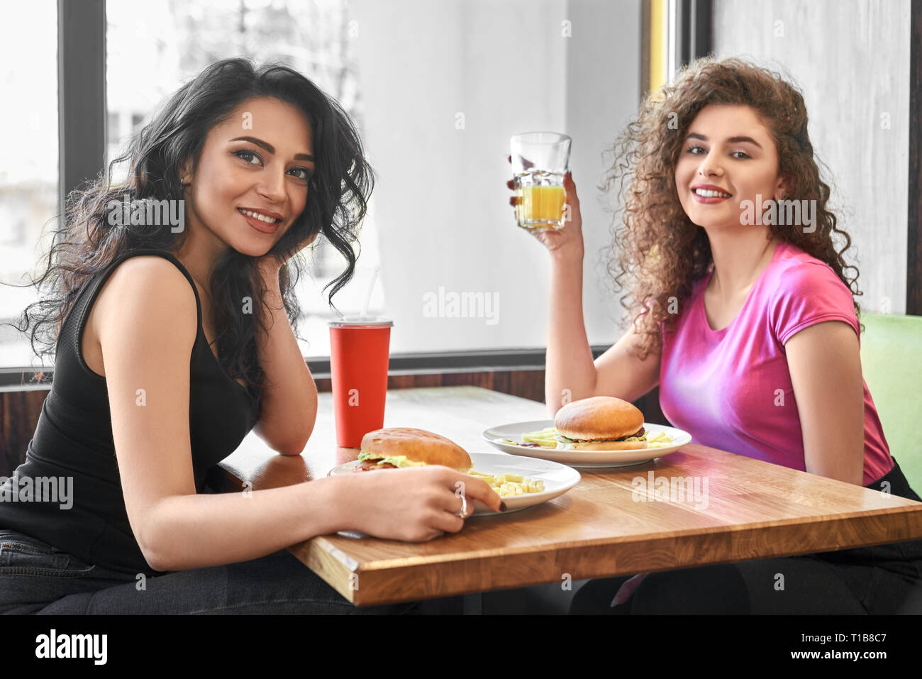 Two beautiful girls in t shirts sitting in cafe near window, posing and ...