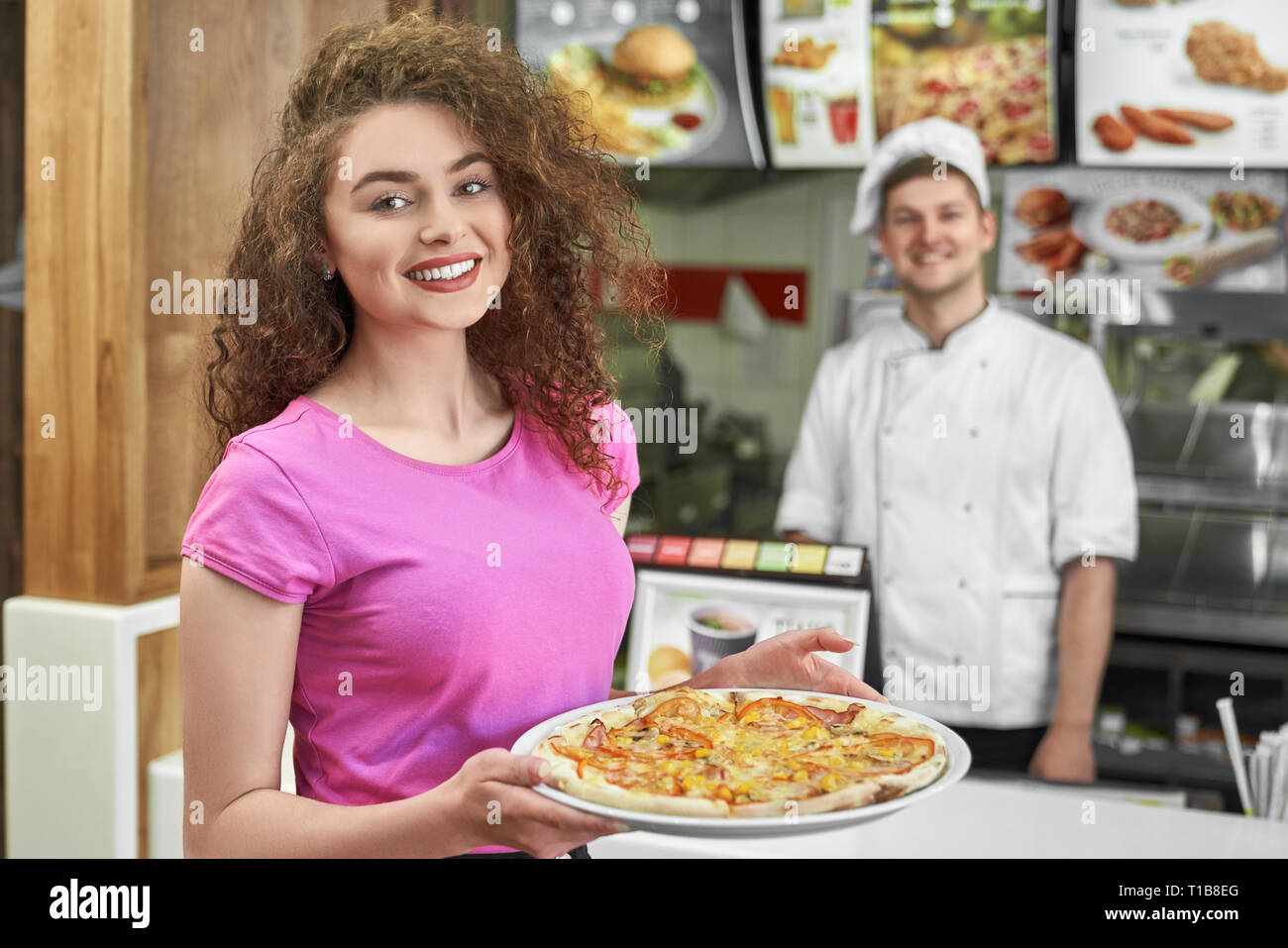 Pretty girl with chestnut curly hair in pink t shirt holding delicious ...