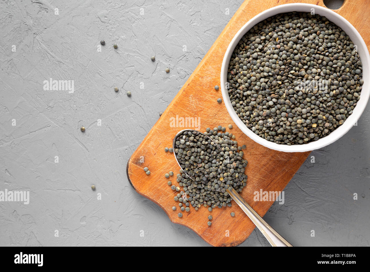 Dry green french lentils in a gray bowl on rustic wooden board, side ...