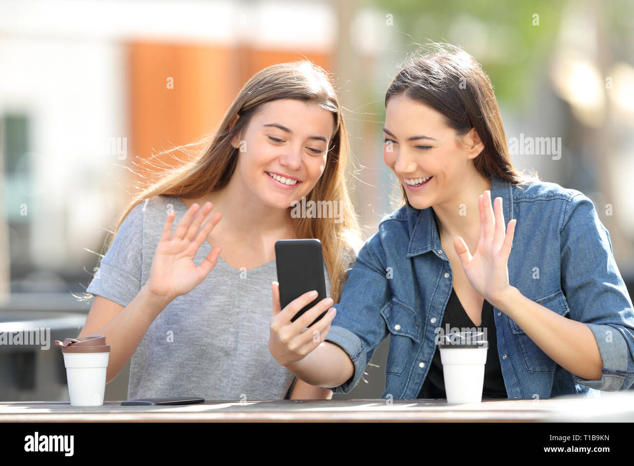 Two happy friends greeting having a video call on smart phone sitting ...
