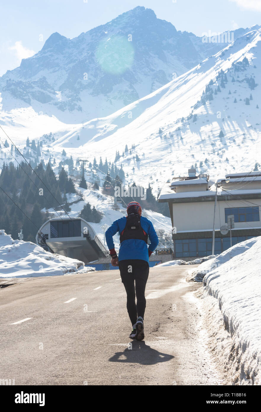 young healthy sport man running on asphalt road at snow mountains in ...