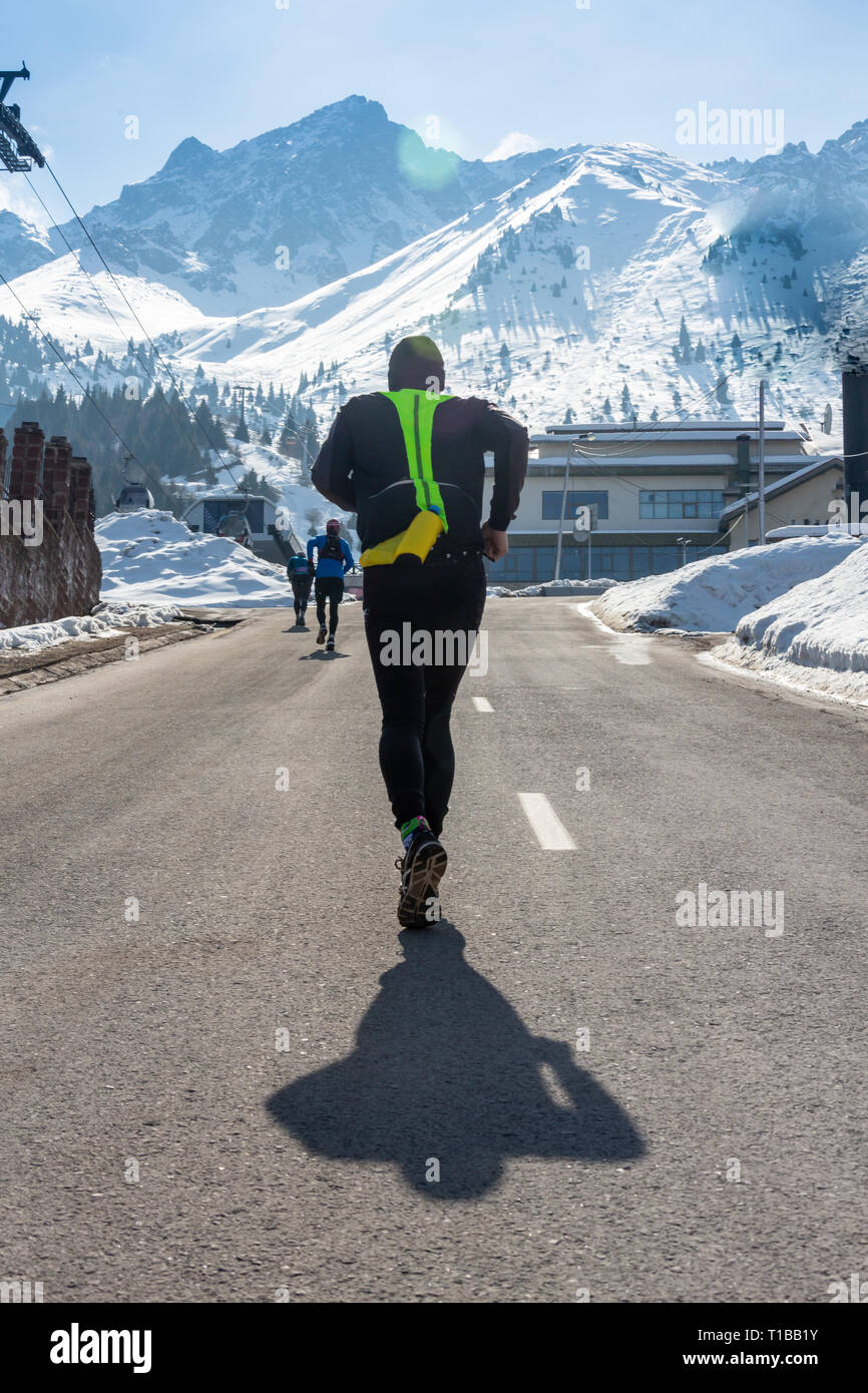 young healthy sport man running on asphalt road at snow mountains in ...