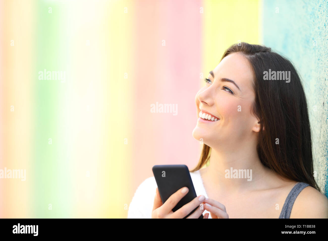 Happy girl holding smart phone thinking looking at side in a colorful ...