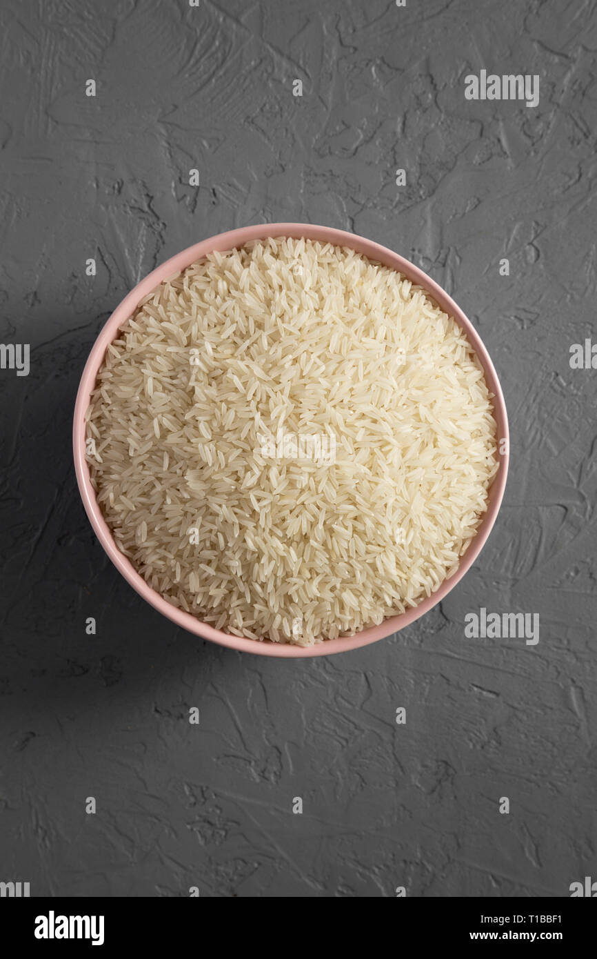 Dry white rice basmati in a pink bowl over concrete surface, top view ...