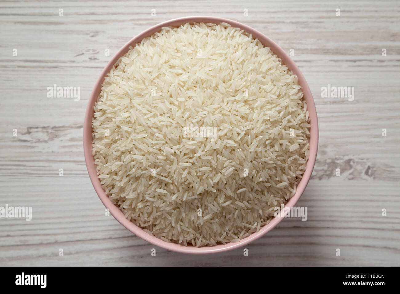 Dry white rice basmati in a pink bowl over white wooden background, top ...