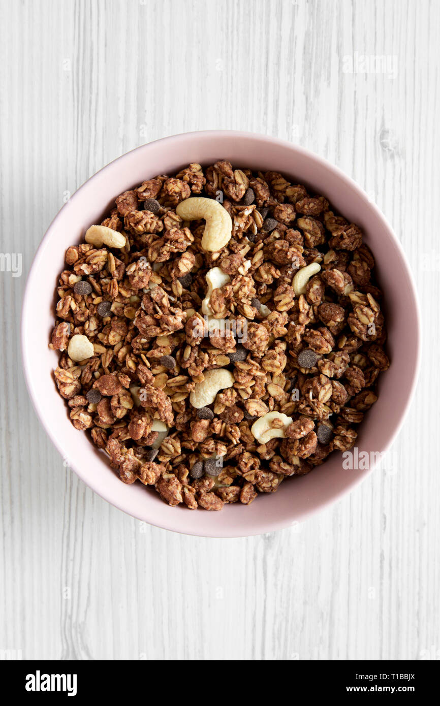 Homemade chocolate granola with nuts in a pink bowl over white wooden ...