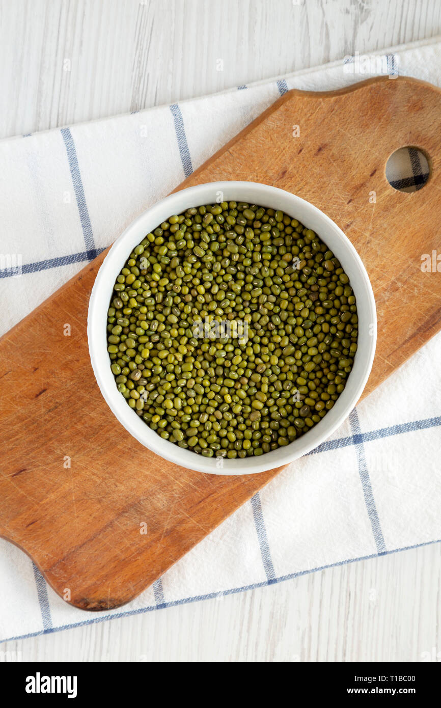 Full bowl of green mung beans on rustic wooden board over white wooden ...