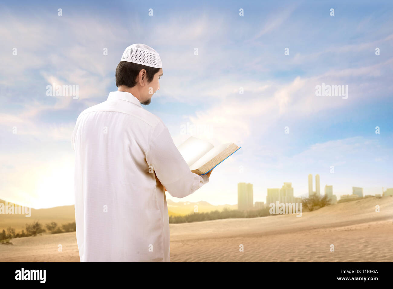 Rear view of asian muslim man with cap standing and reading the quran ...