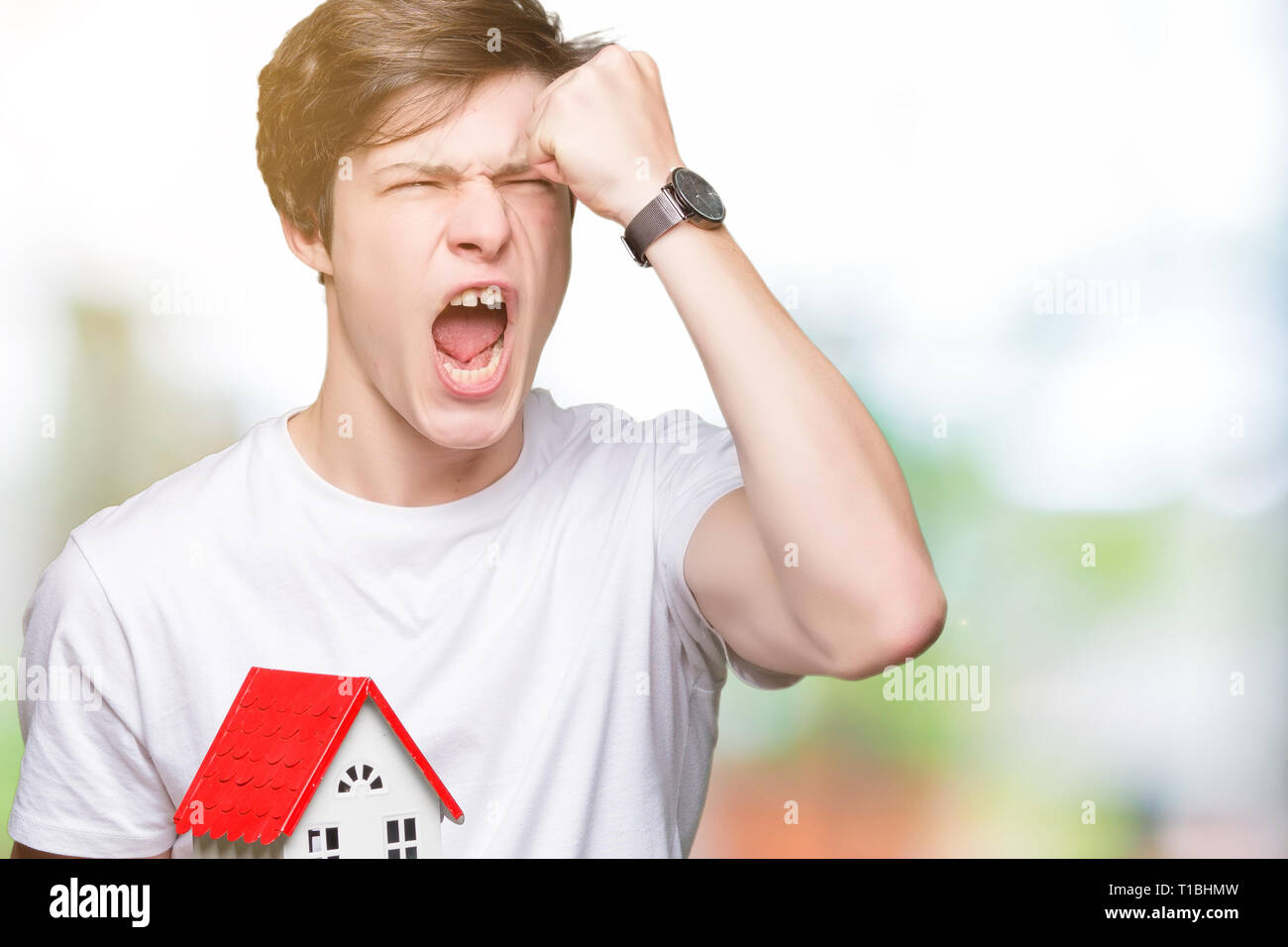 Young man holding house over isolated background annoyed and frustrated ...