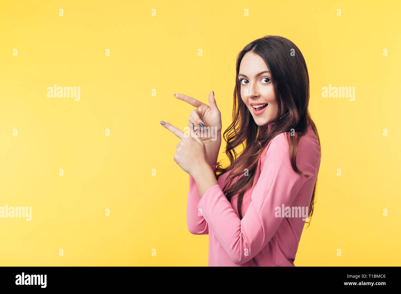 Beautiful smiling woman showing empty copy space pointing her fingers isolated on yellow ...