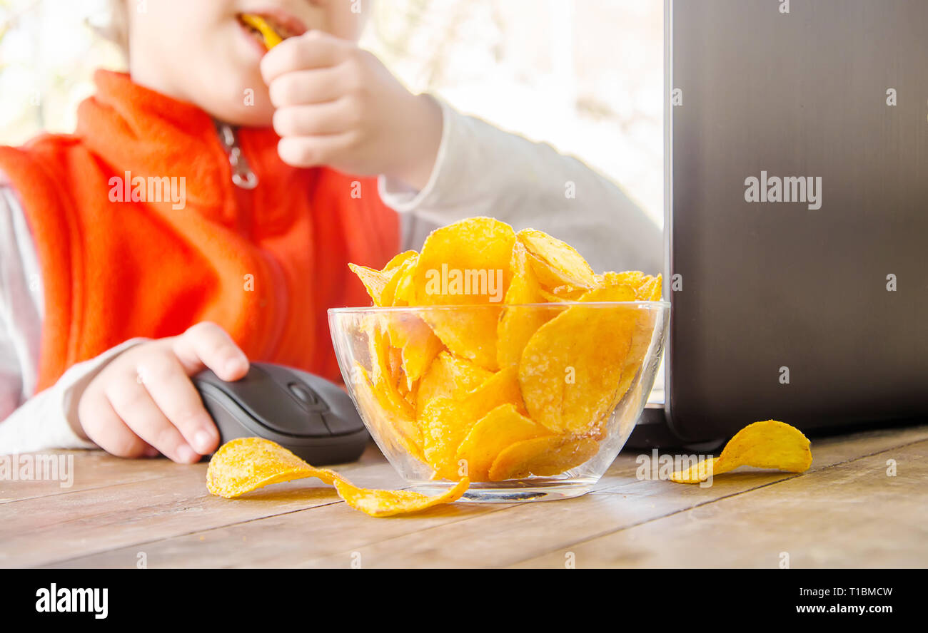 child with chips behind a computer. selective focus. food Stock Photo ...