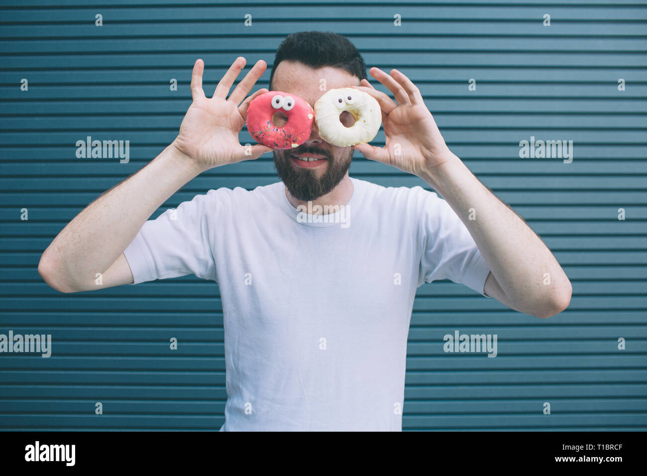 Funny picture of man holding two colorful donuts around his eyes. He is ...